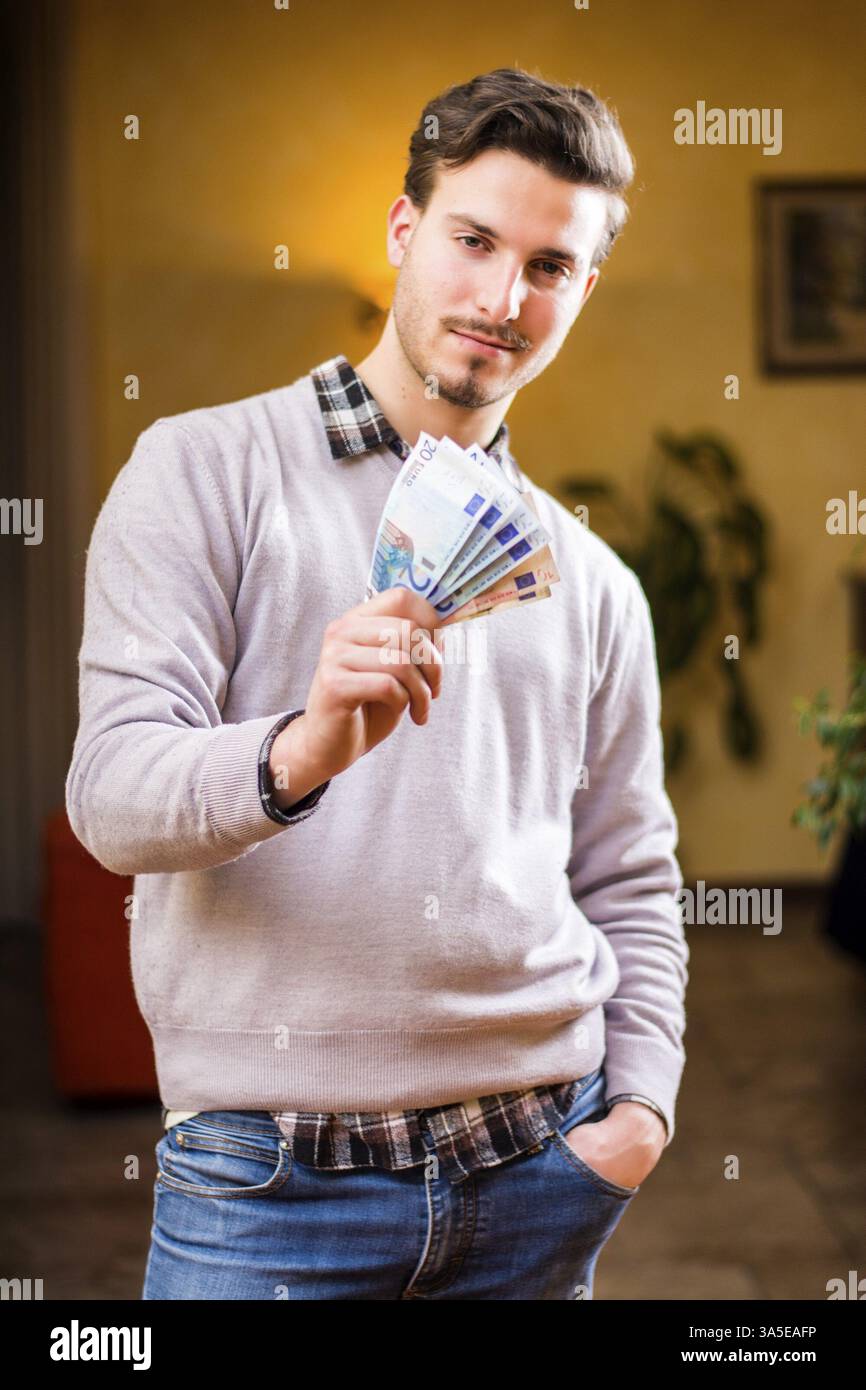 Handsome young man counting money, standing at home in his living room ...