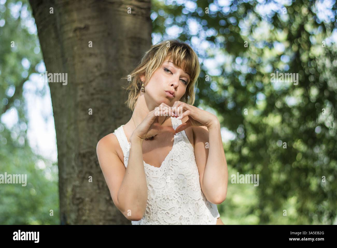 Pretty blonde young woman doing heart sign with hands as a symbol of ...