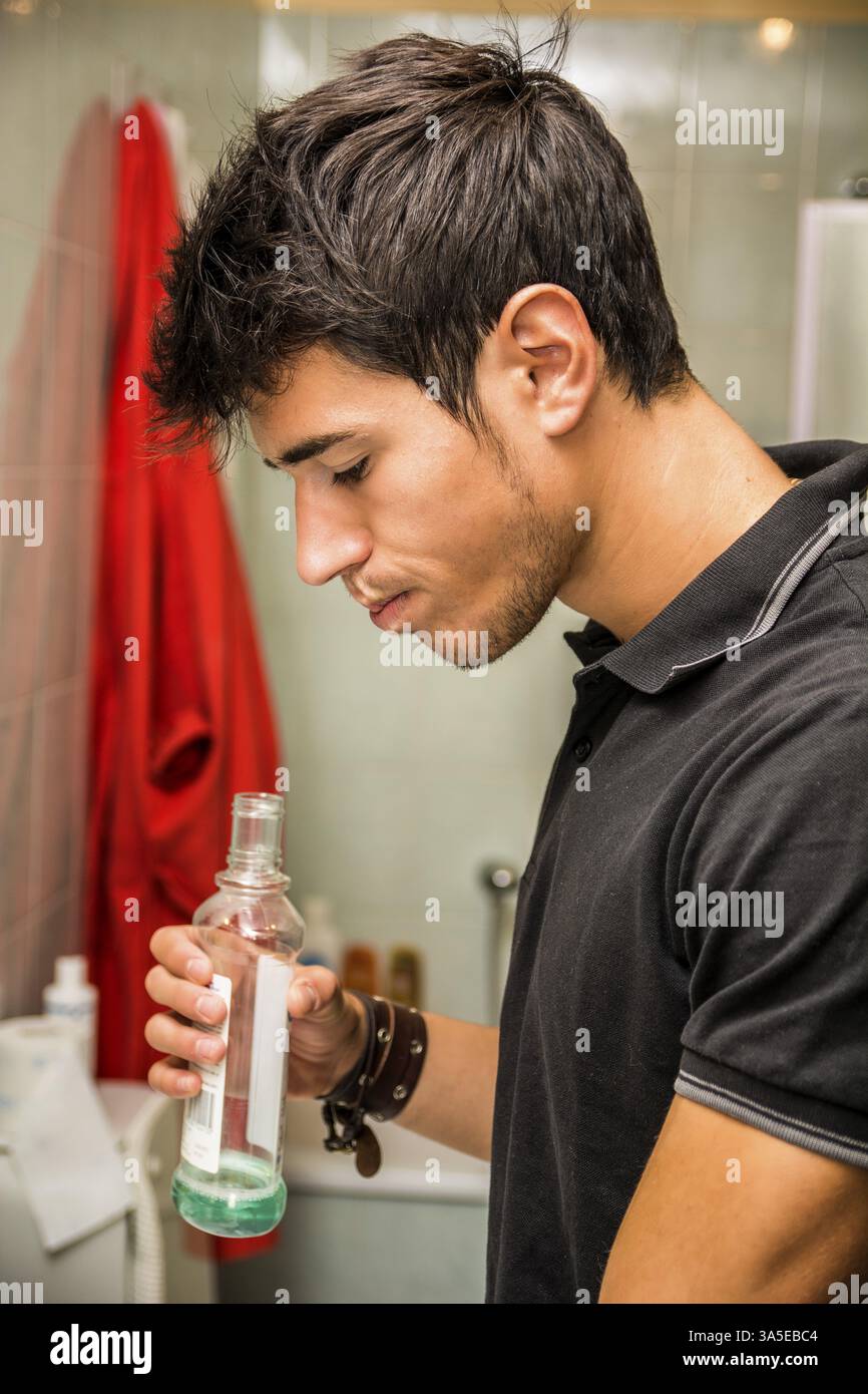 Handsome young man using mouthwash to clean his teeth and mouth, in his ...