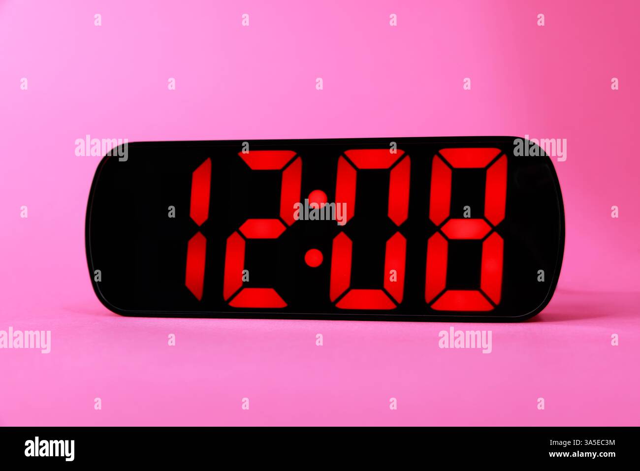 Digital alarm clock showing 12:08 o'clock on pink background, closeup ...