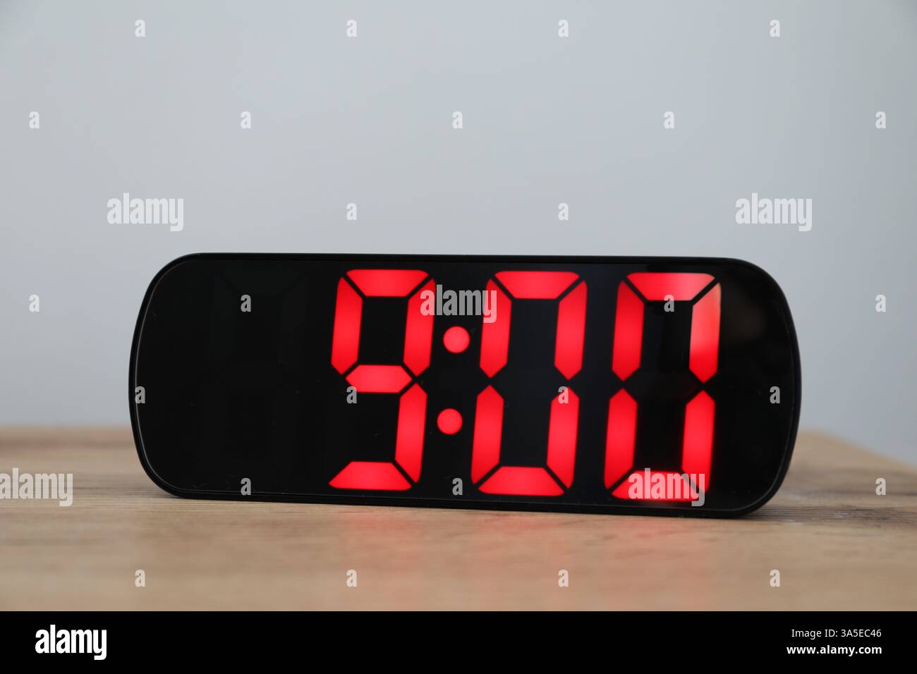 Digital alarm clock showing 9:00 o'clock on bedside table against light ...