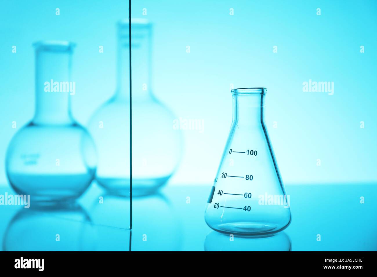 Empty flasks on mirror surface against light blue background ...