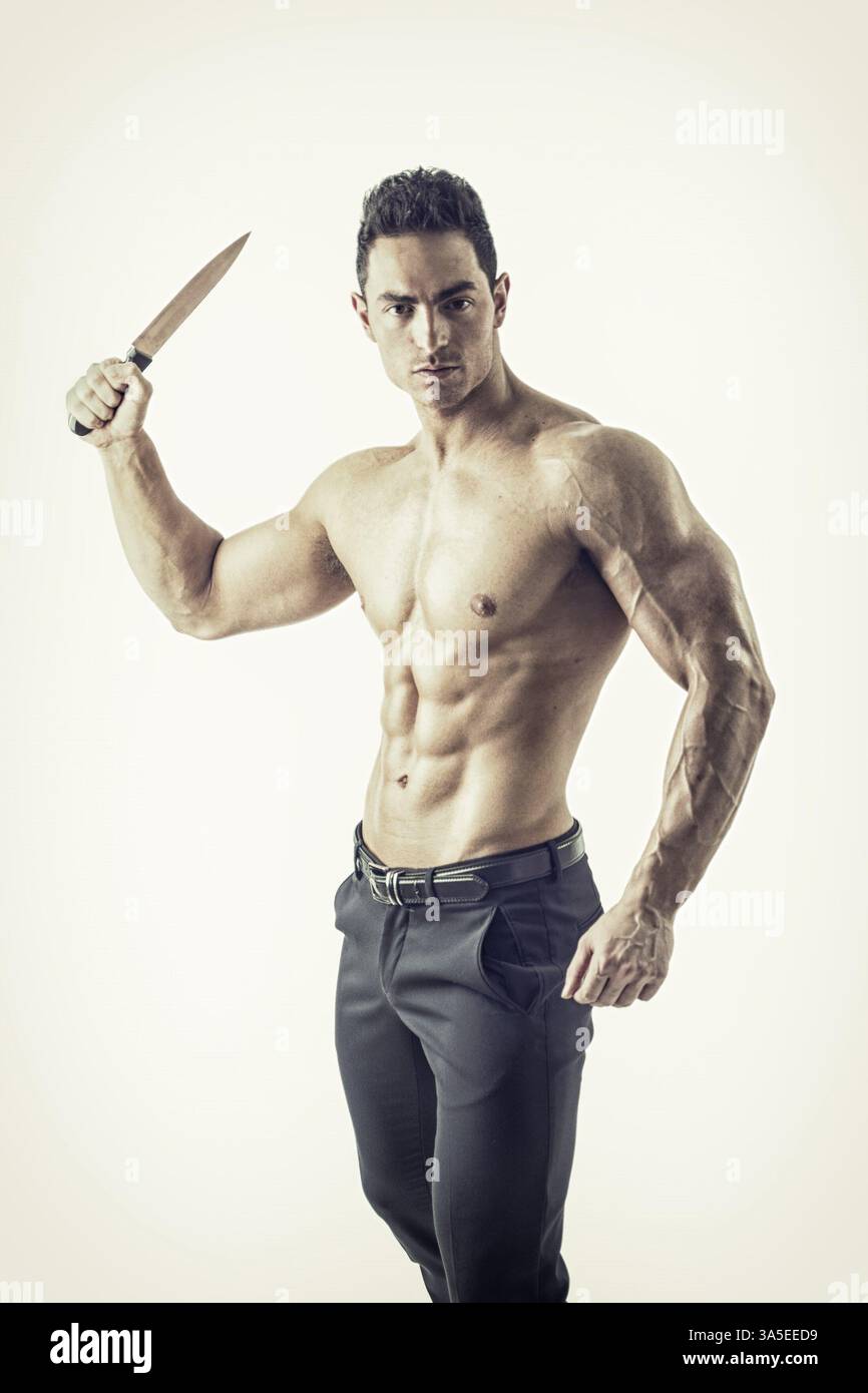 Muscular young man holding big knife ready to stab, isolated on white ...