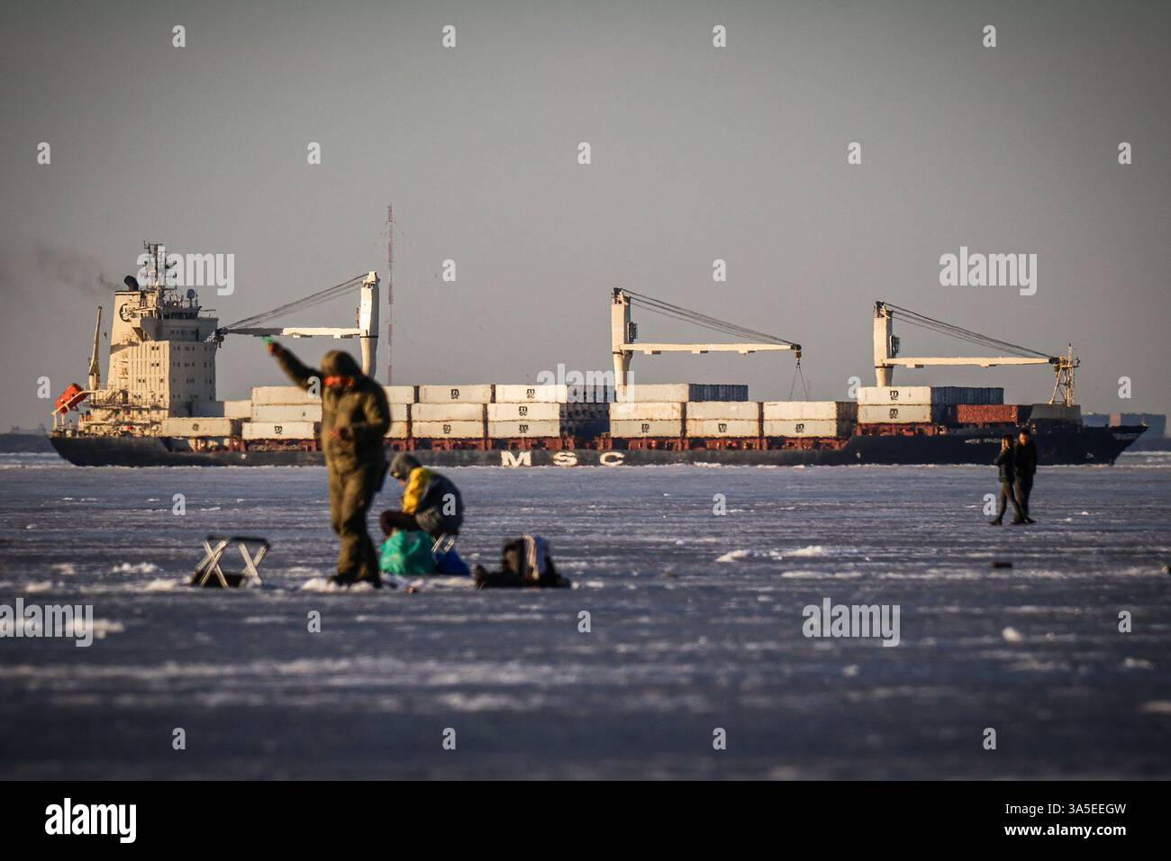 Fishermen sit on the ice of the Gulf of Finland against the backdrop of the container ship MSC ...