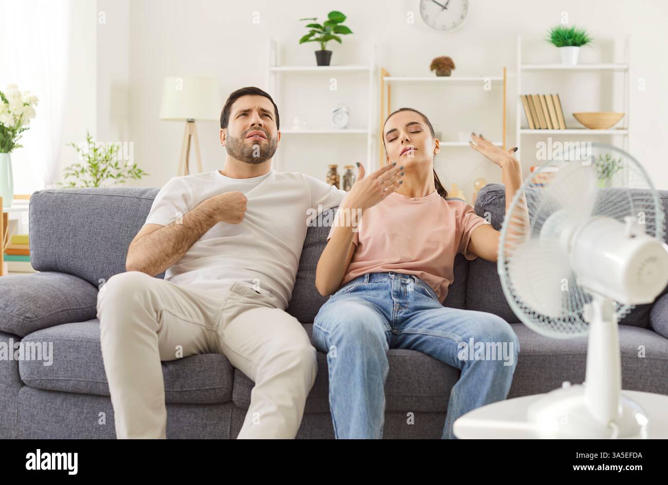 Young couple being exhausted of summer heat, using electric fan to make ...