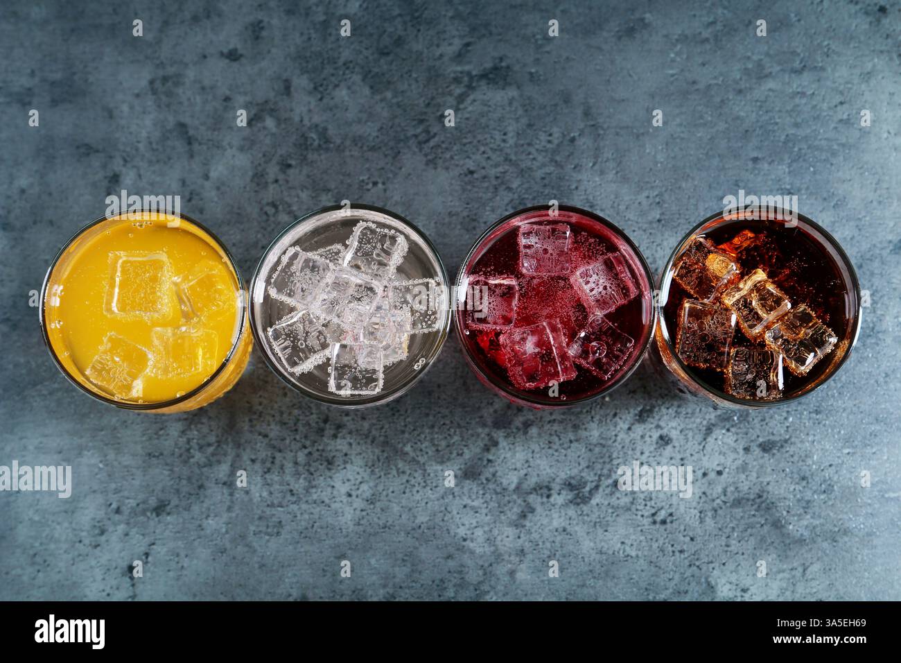 Sweet soda water of different flavors with ice cubes in glasses on grey table, flat lay Stock ...