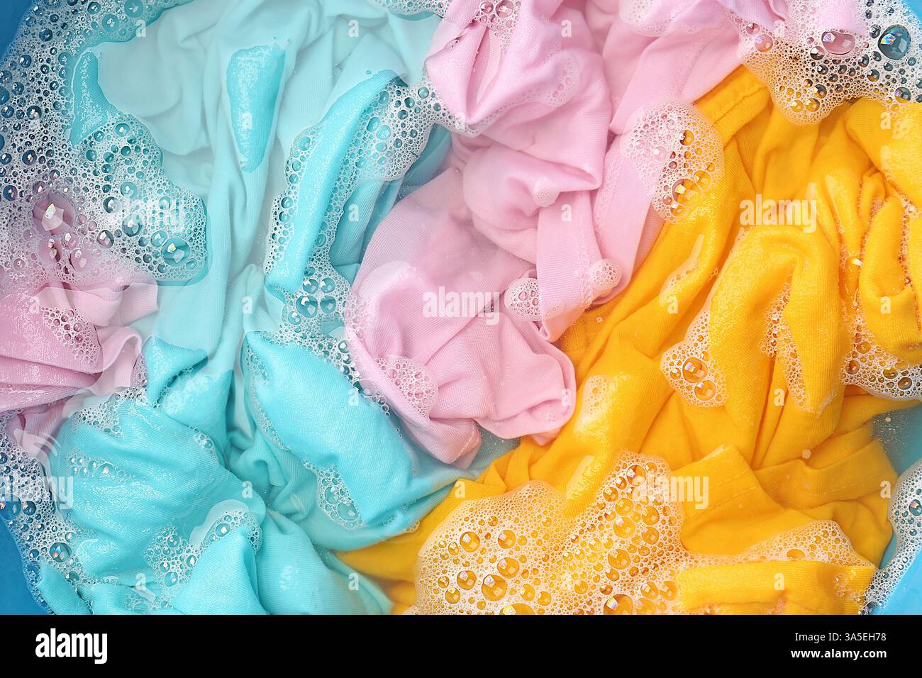 Colorful clothes soaked in water before washing, top view Stock Photo ...