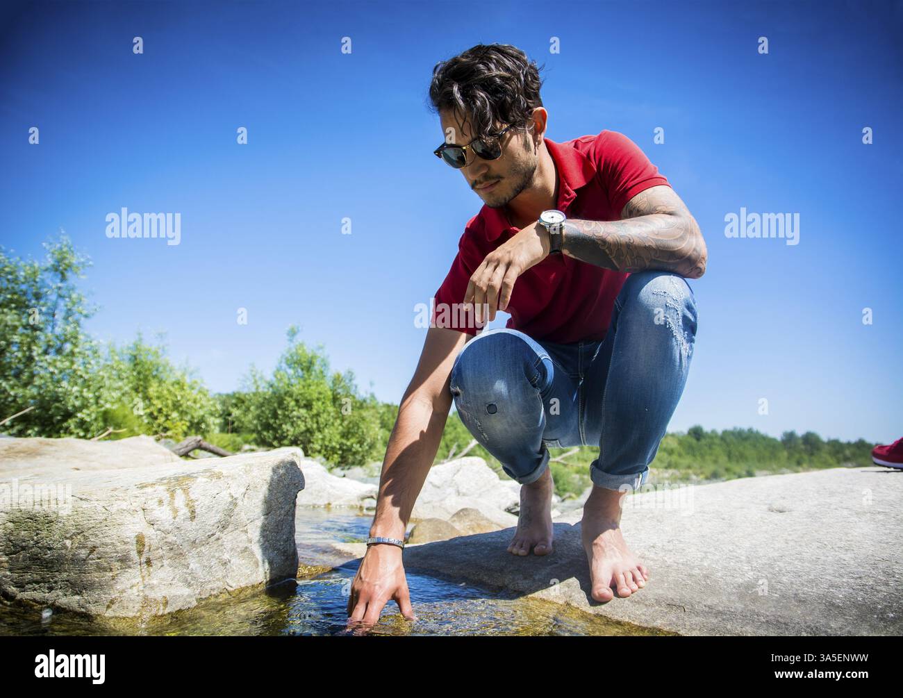 Attractive young man outdoor at river or water stream, sitting on big ...