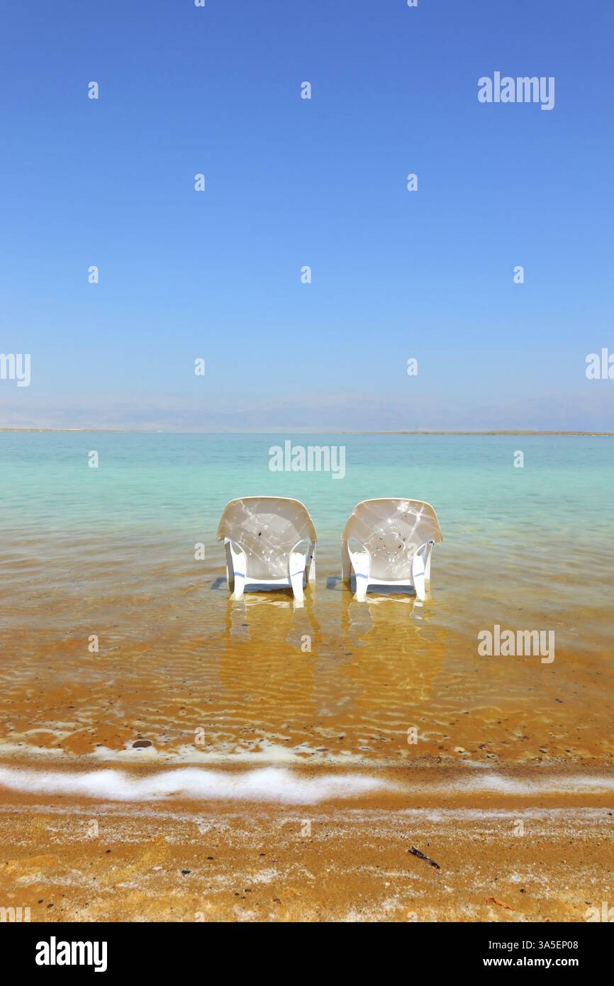 Two white beach chairs stand near the water at the beach. Dead Sea ...