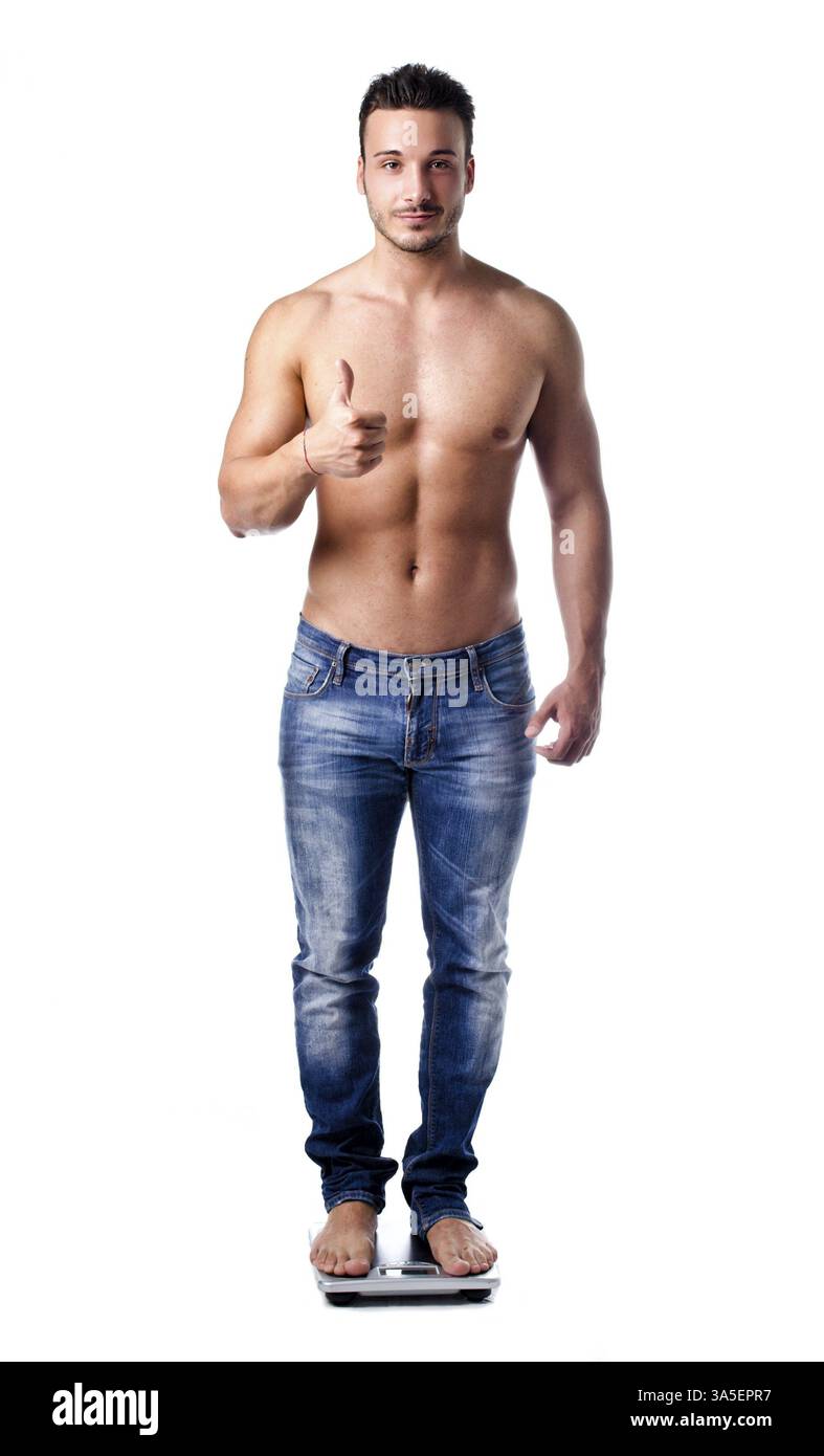 Muscular young man weighing himself on scale, making OK sign with thumb ...