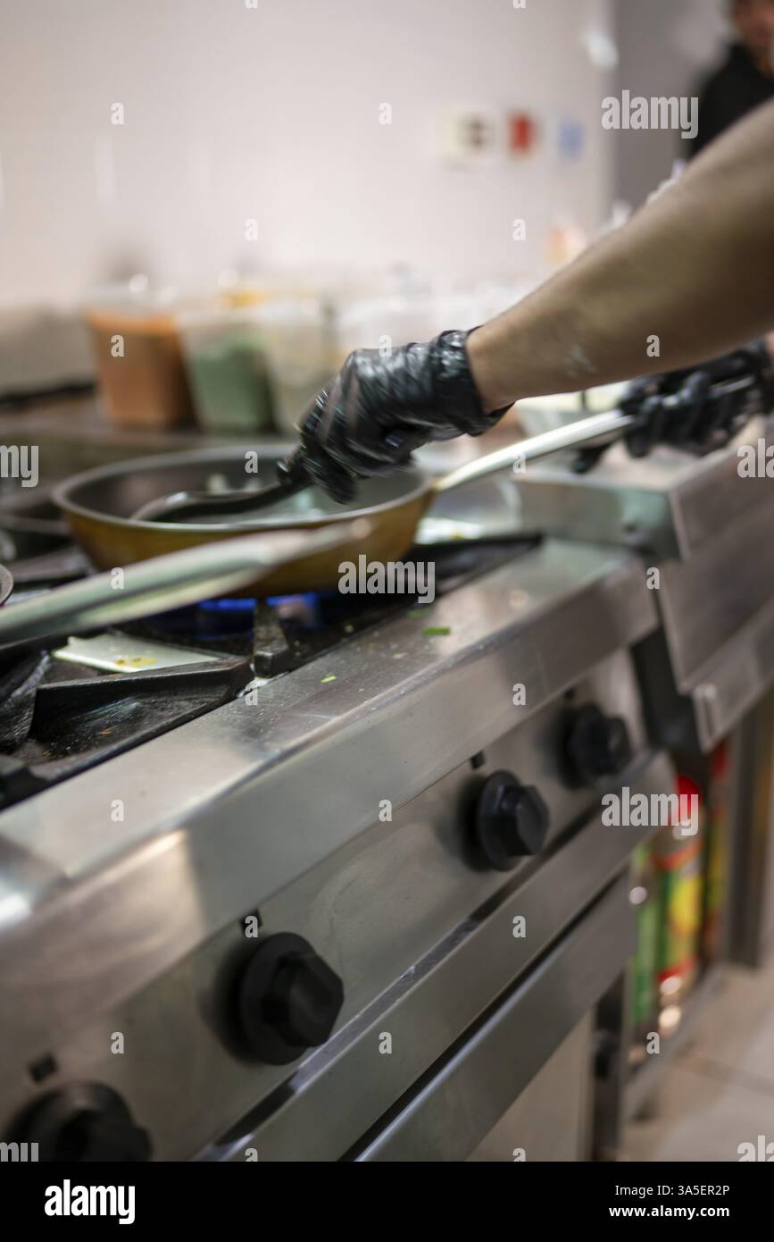 A gloved hand maneuvering a frying pan over a stove, showcasing active ...