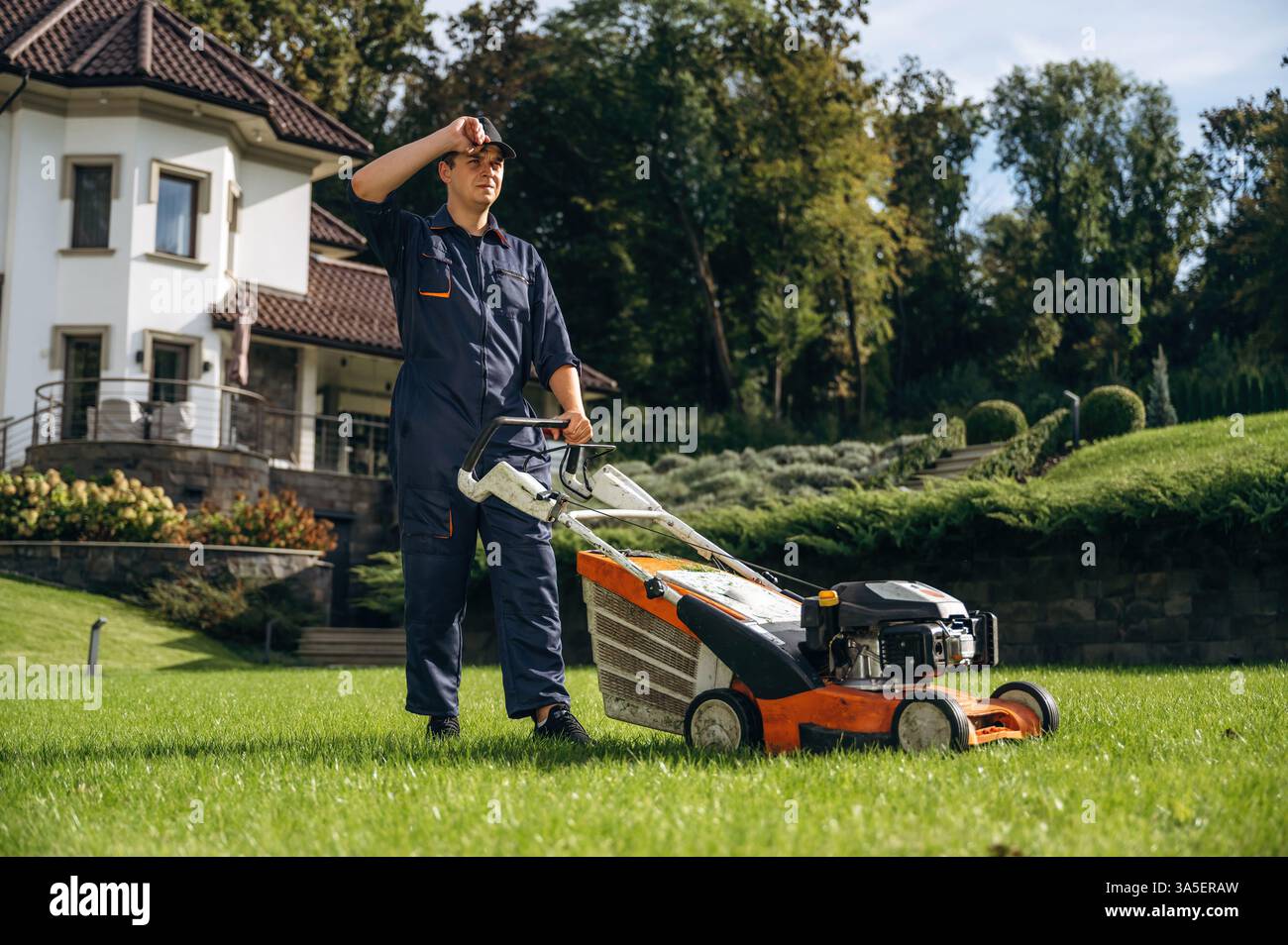 Cutting the grass by lawn mover. Professional gardener is on the lawn ...