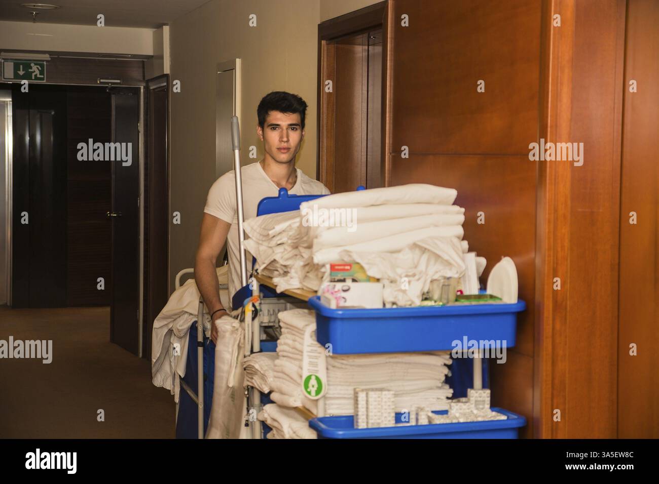 Young man pushing a housekeeping cart laden with clean towels, laundry ...