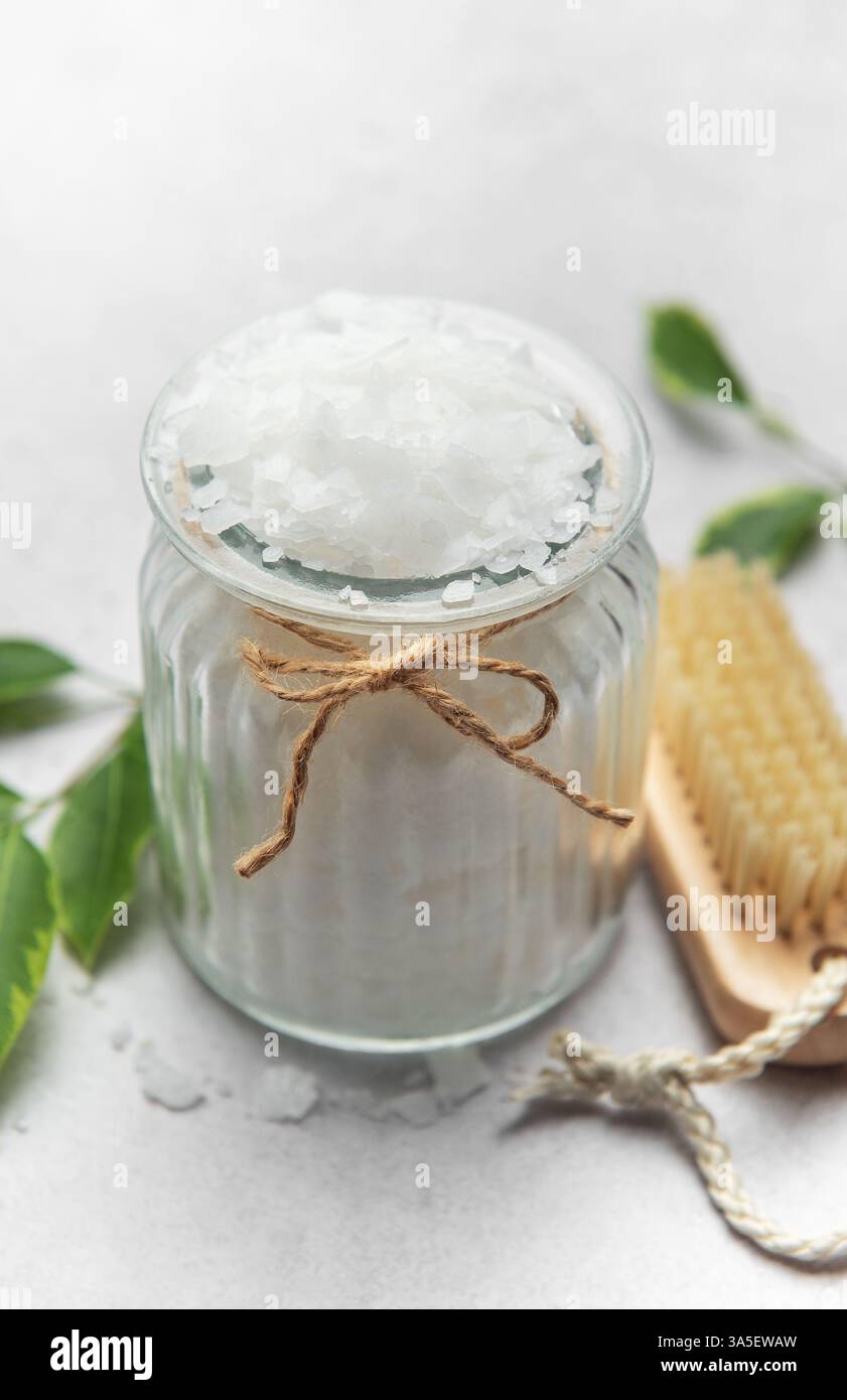 Magnesium bath flakes in glass jar, wooden brush and green leaves ...