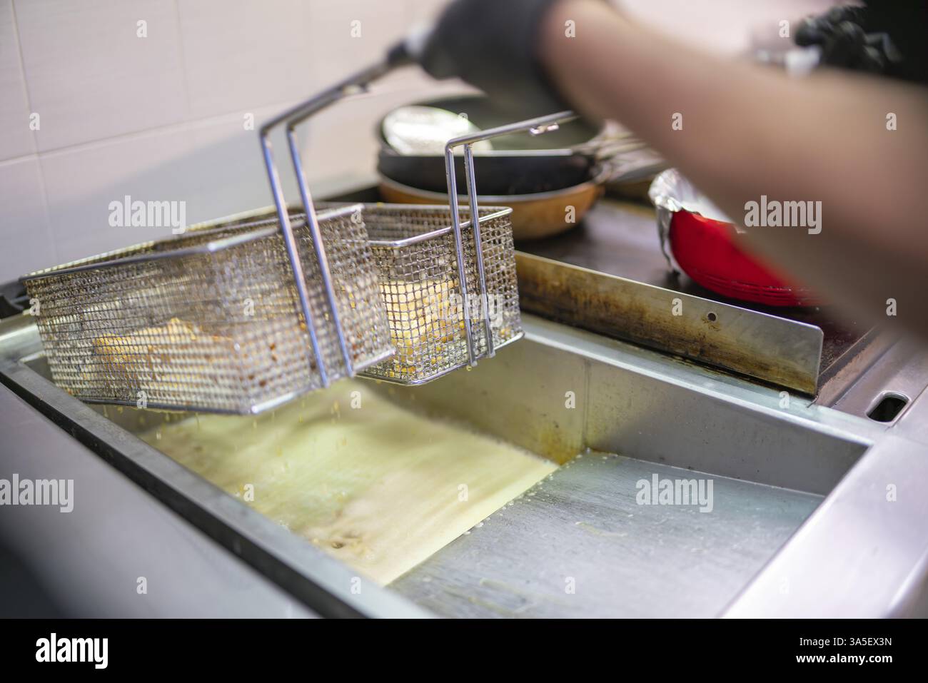 Metal fry baskets filled with samosas dripping oil into a deep fryer in ...