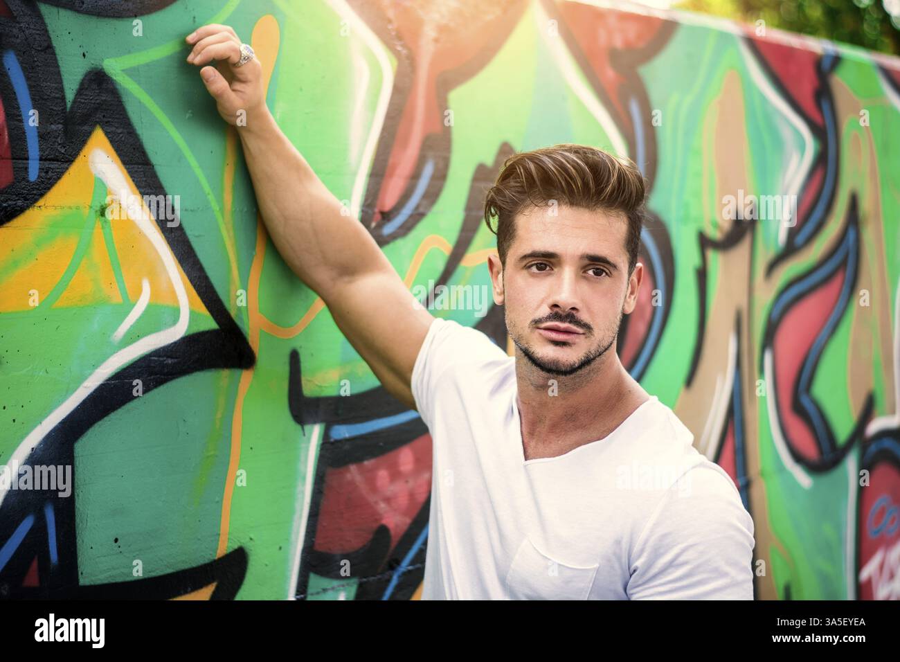 Attractive muscle man leaning on colorful graffiti wall, wearing white ...