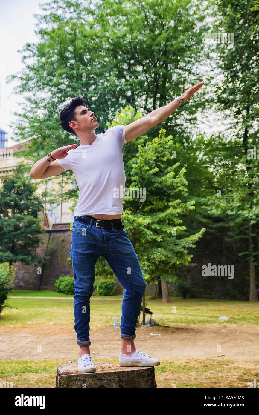 Side view of young man posing on stump imitating statue Stock Photo - Alamy