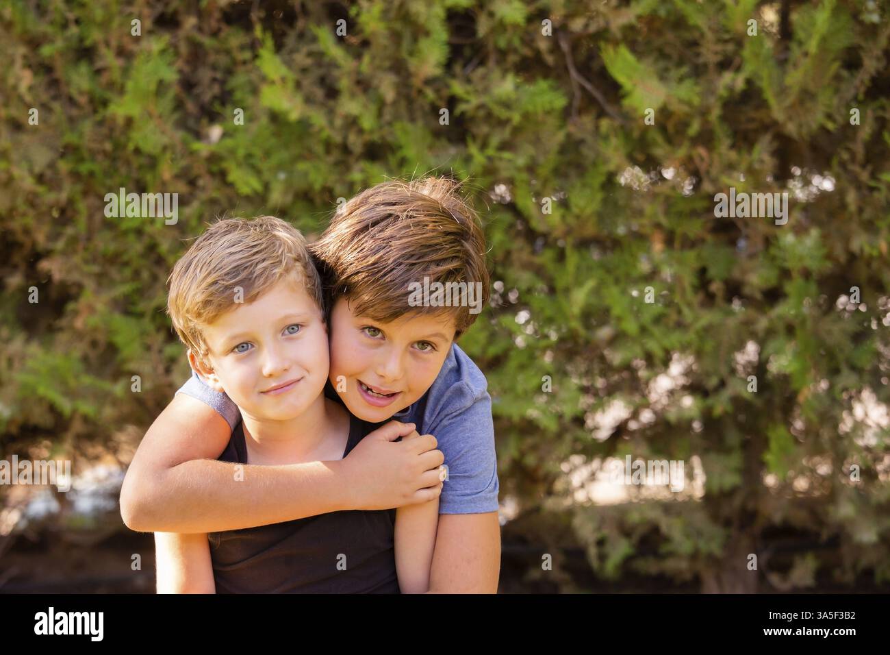 Two wonderful boys are hugging. The older brother has brown hair and ...
