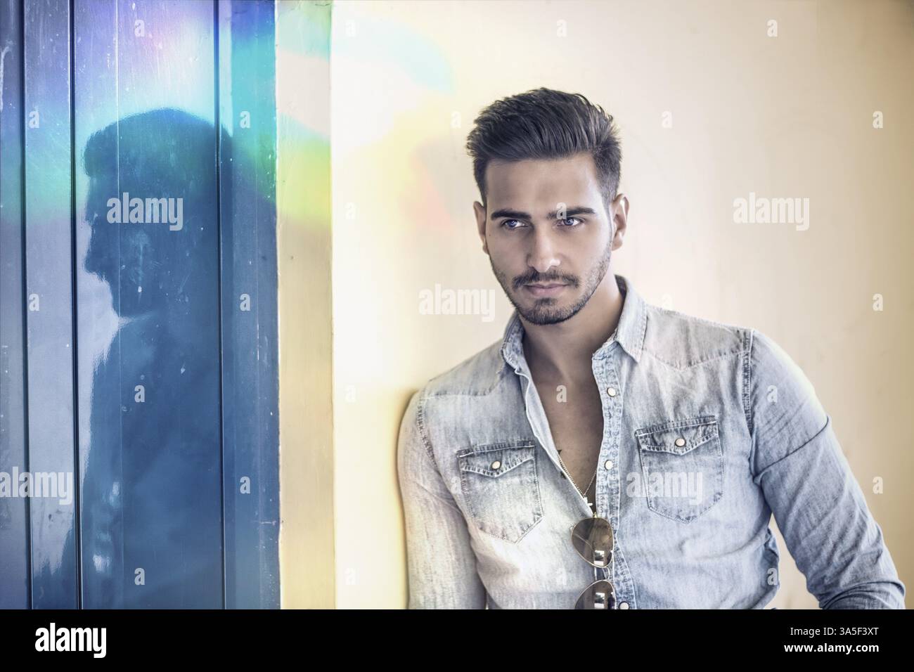 Attractive young man standing against colorful wall, looking at camera ...