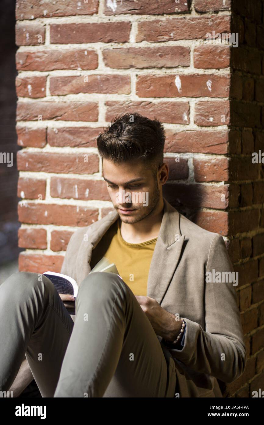 Male student reading book outdoor. Handsome young man reads a book ...