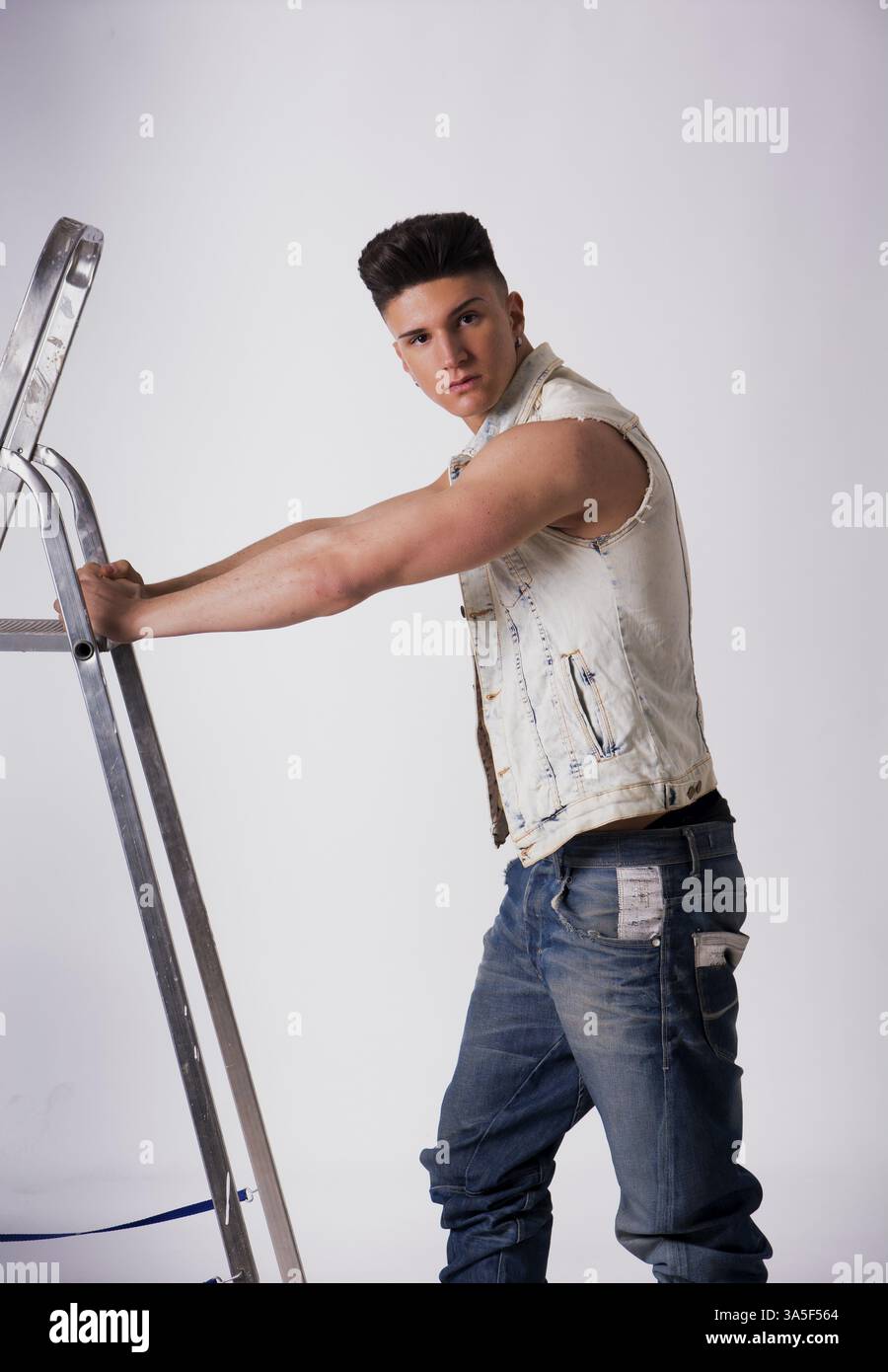 Attractive young man leaning on metal ladder, looking at camera, on ...