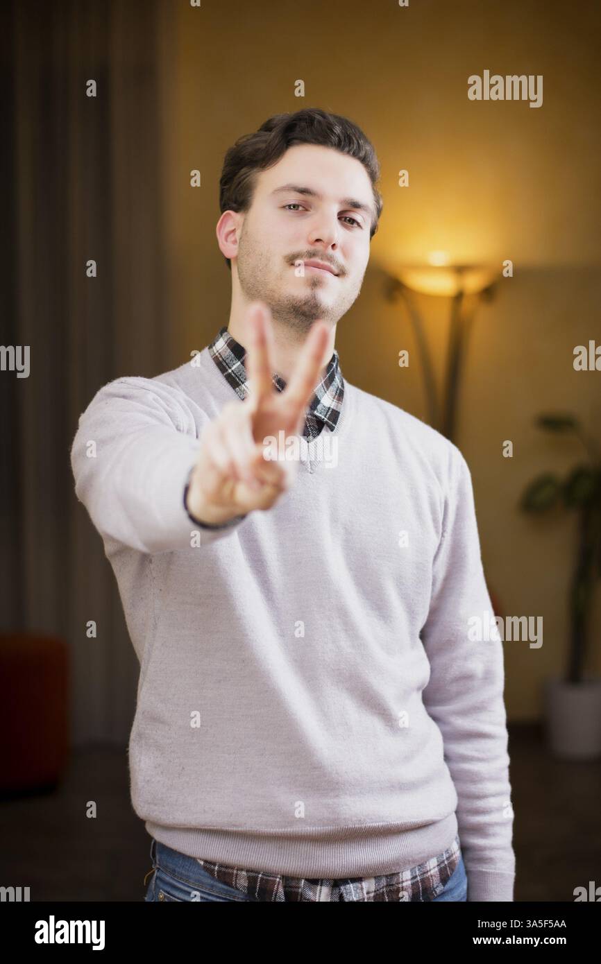 Attractive young man doing peace or victory sign with two fingers ...