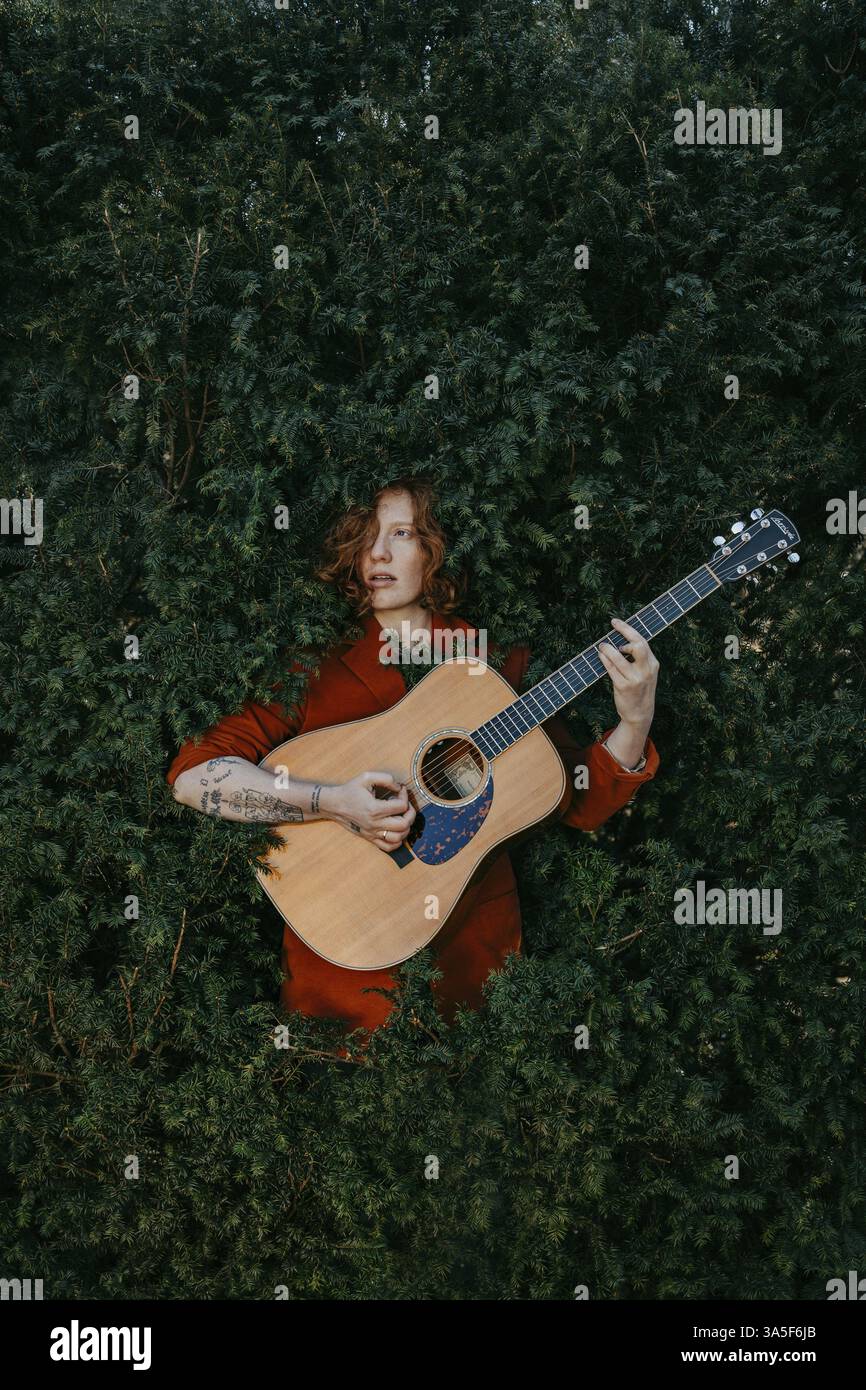 Red-haired guitarist with guitar in the green bush Stock Photo - Alamy