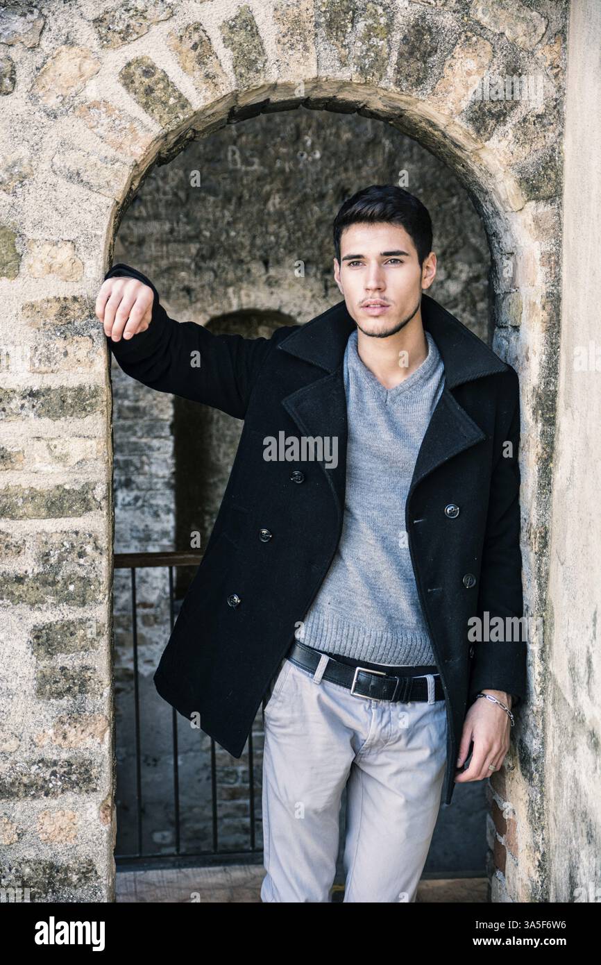 Attractive young man standing against brick wall, in historic building ...