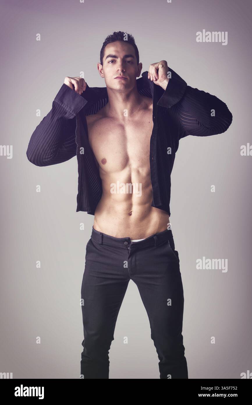 Handsome muscular young man taking off shirt, on light grey background ...