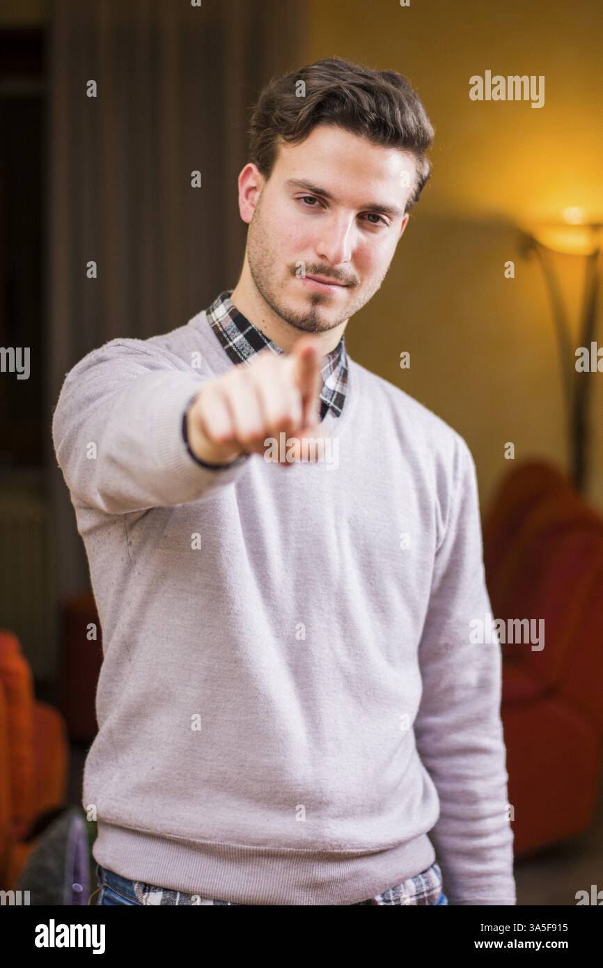 Handsome young man pointing finger at you, smiling. Indoors shot inside ...
