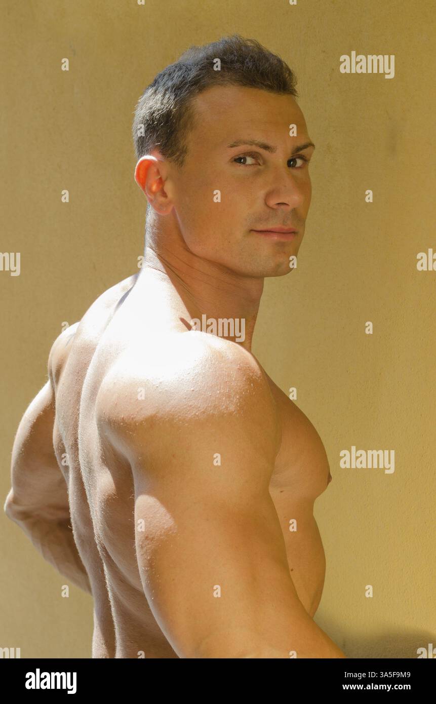 Attractive and muscular male bodybuilder standing next to yellow wall ...