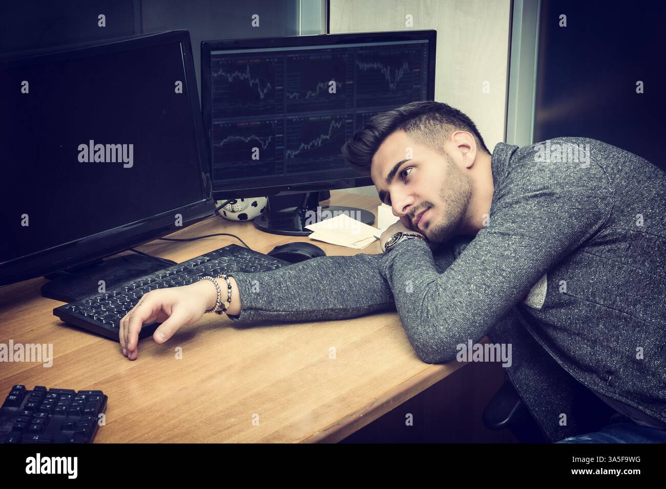 Tired bored sleepy young businessman or office worker sitting at his desk in front of his ...