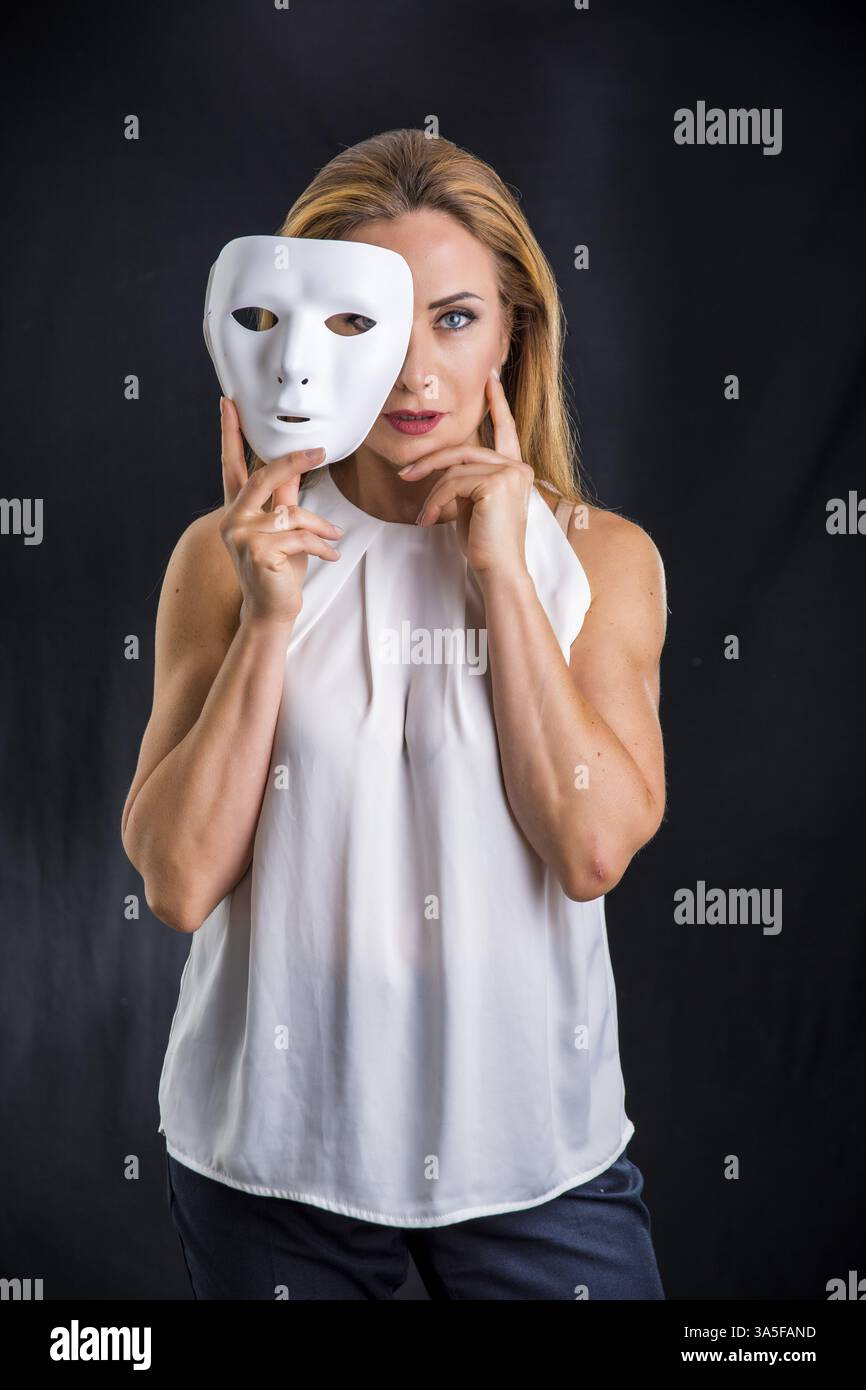 Attractive woman holding theatre mask against black background in ...