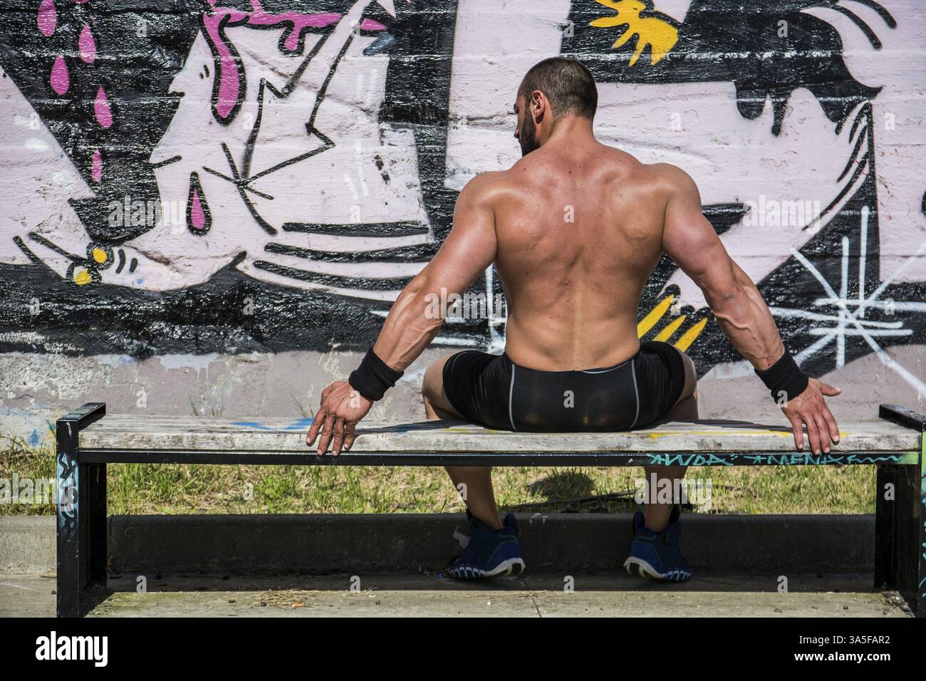 Photo of a muscular man sitting on a bench with vibrant graffiti in the ...