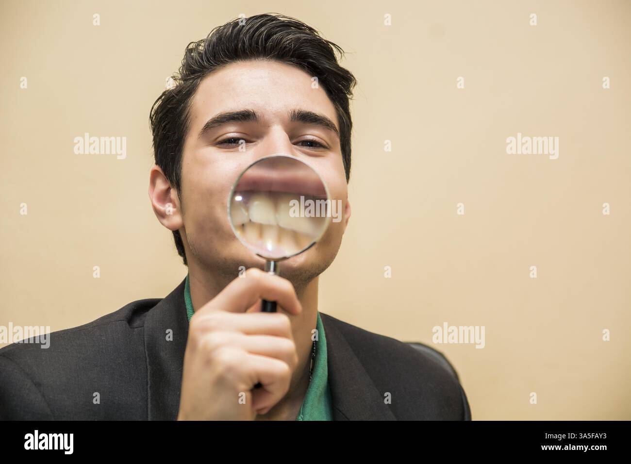 A young man exposing his teeth and mouth through a magnifying glass and ...