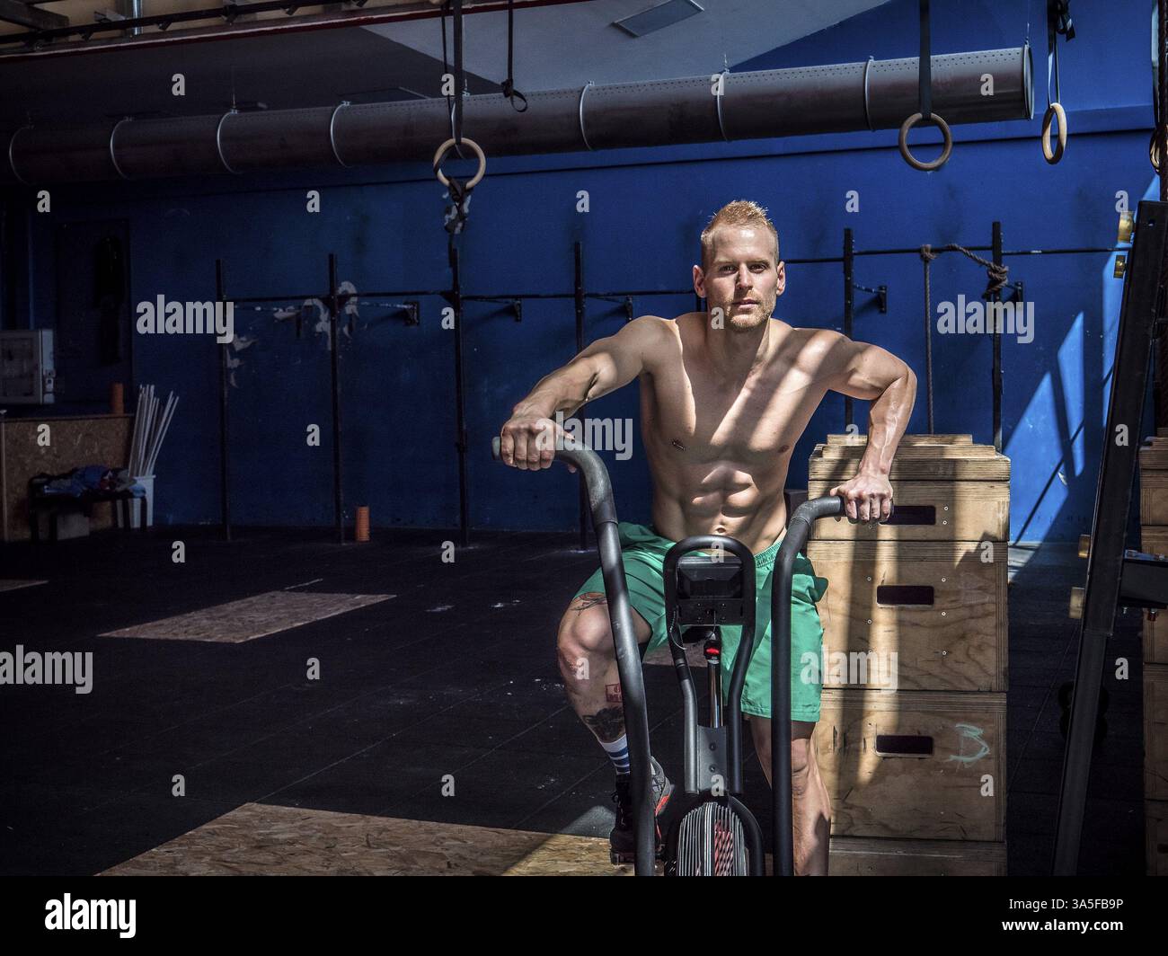 Hunky muscular blond male bodybuilder exercising on stationary bike in ...