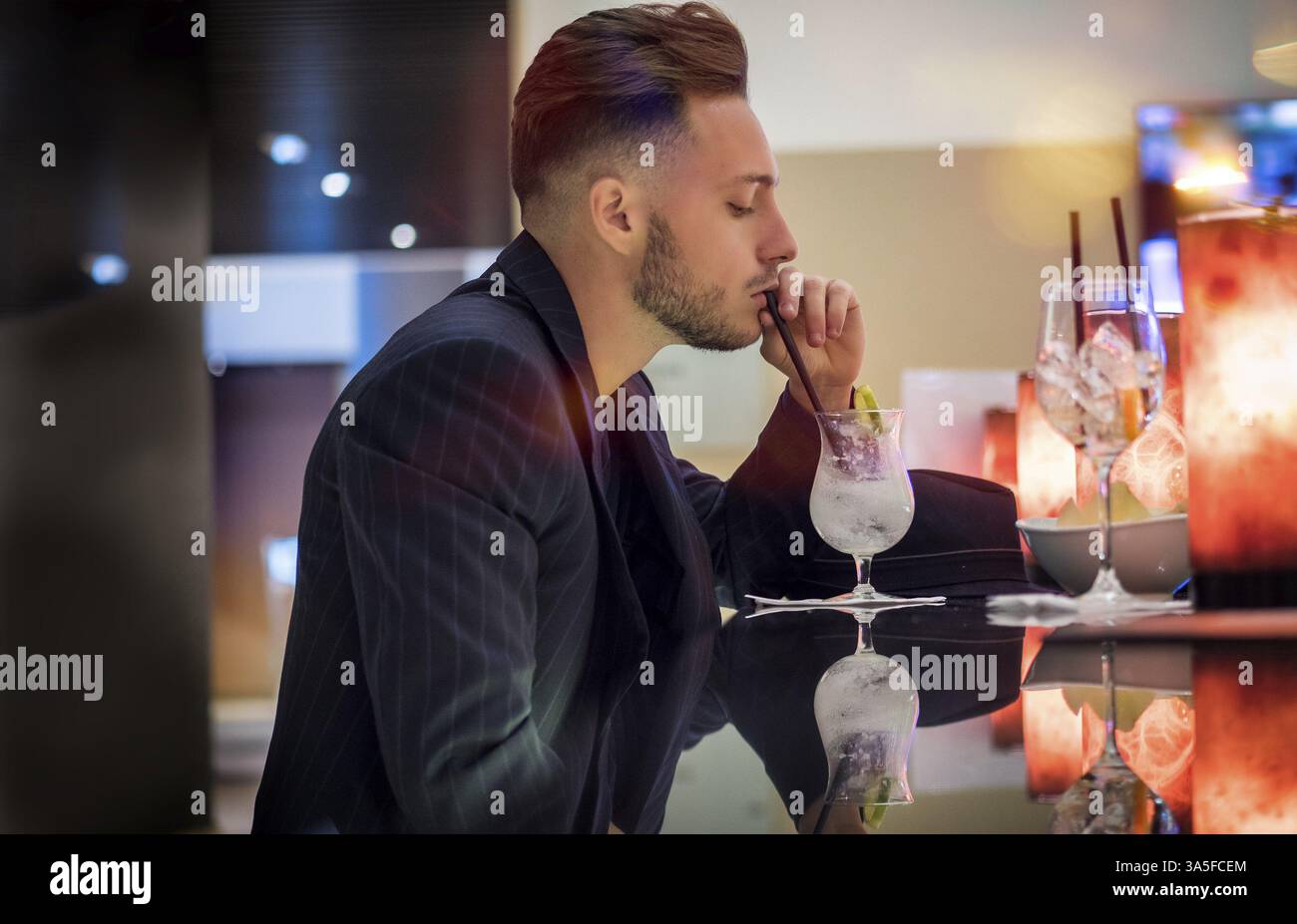 Handsome young man drinking cocktail at bar counter, wearing business ...