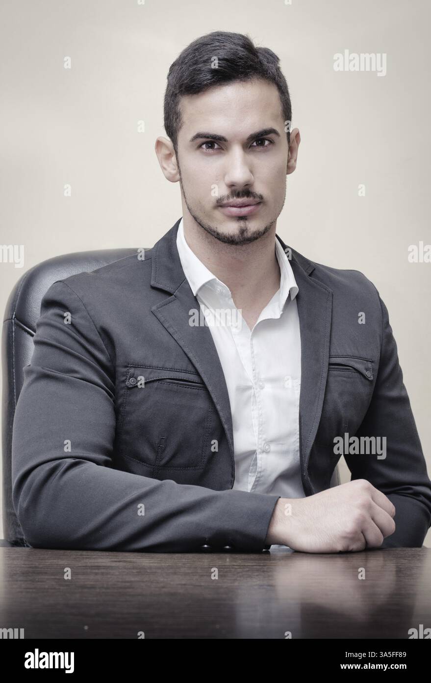 Serious, handsome young office worker in shirt and jacket at his desk ...