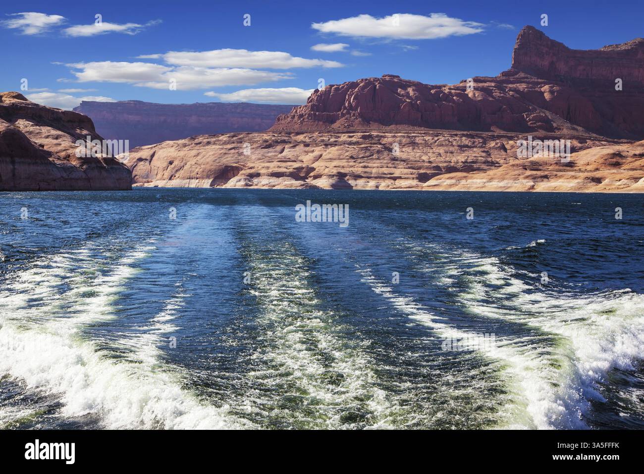 Foamy trace of a motor boat crosses the emerald waters. Red sandstone ...