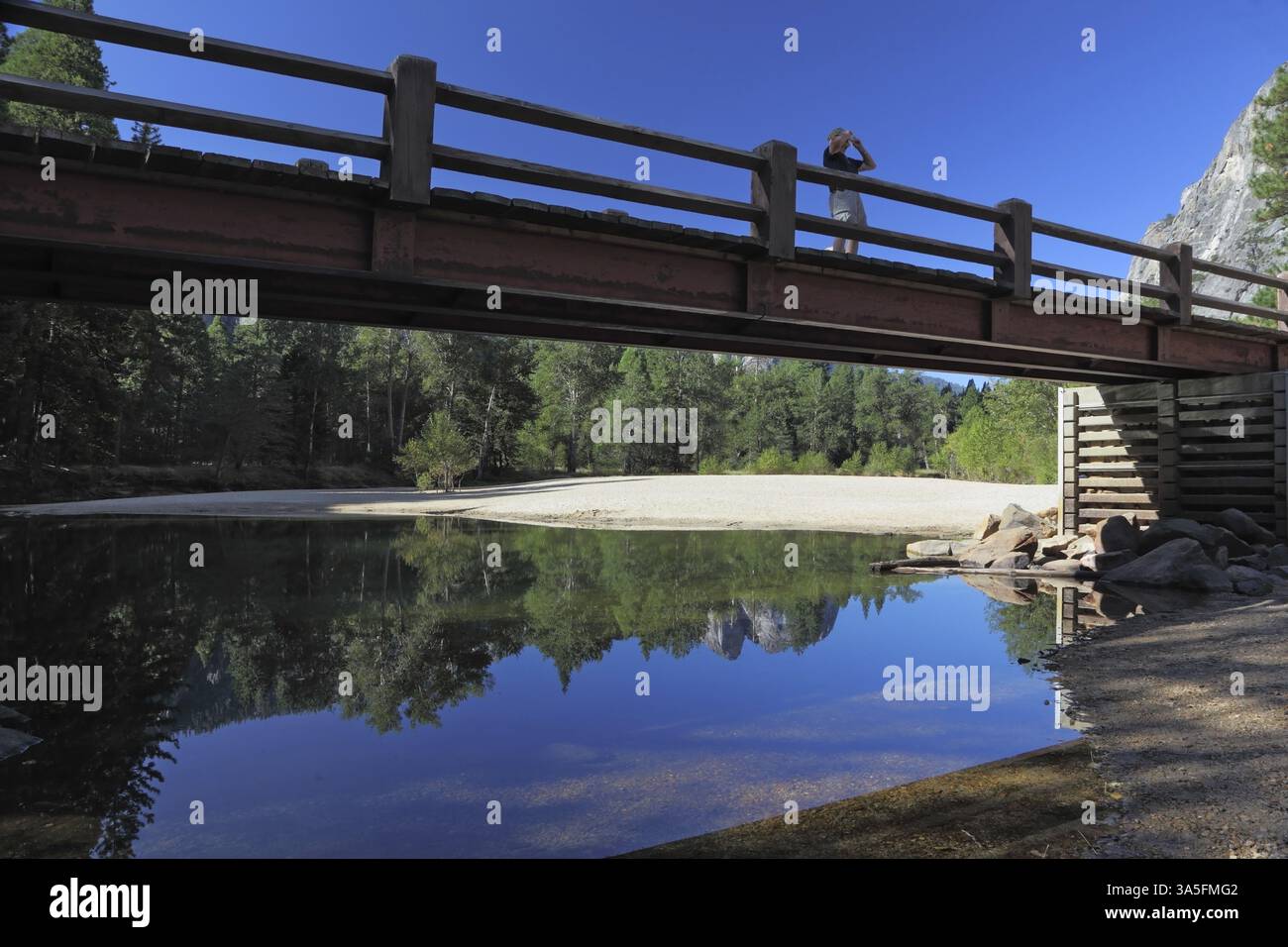 Wooden footbridge over the Merced River in Yosemite Park. In the still ...