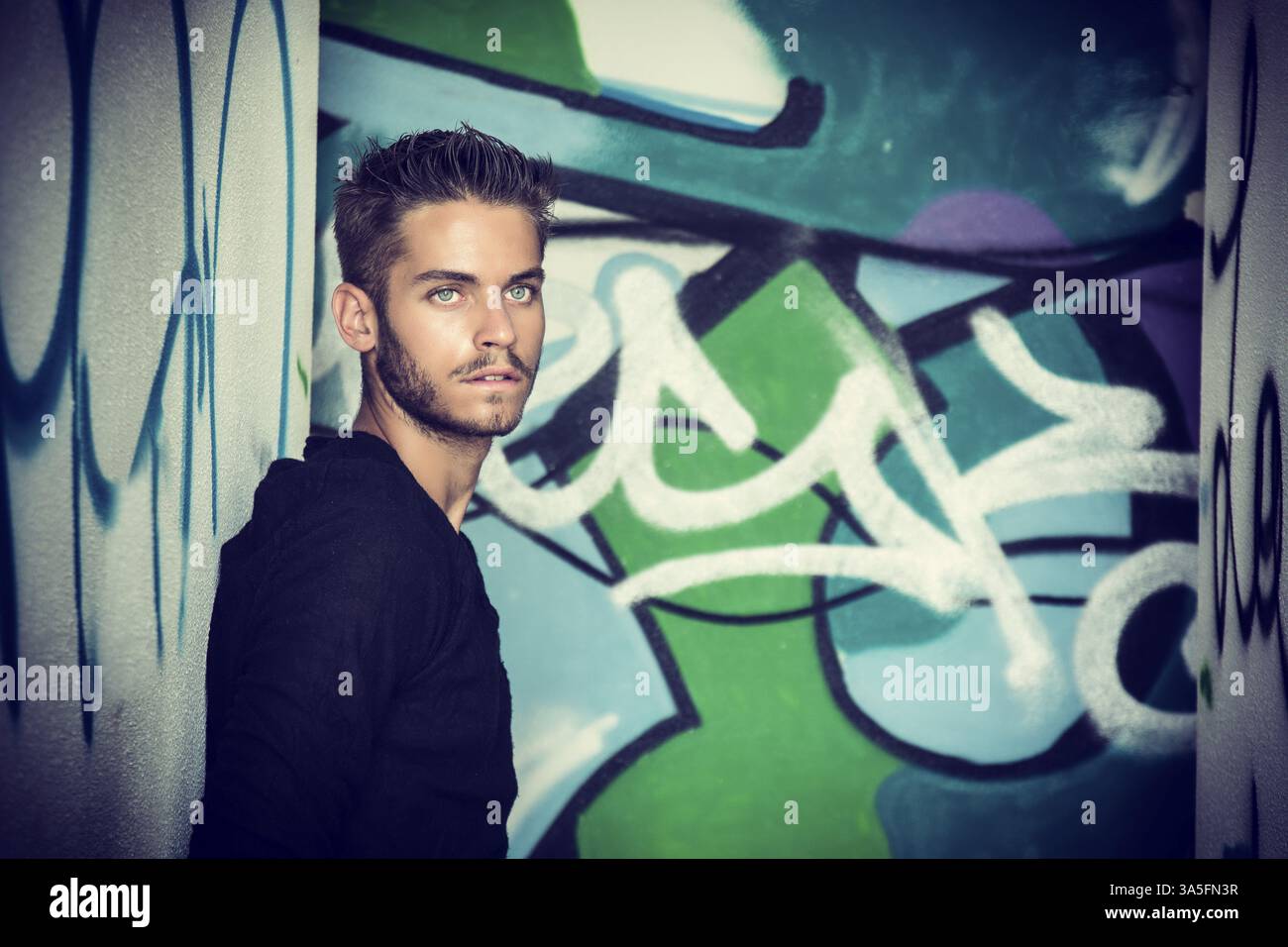 Attractive young man standing against colorful graffiti wall, looking ...