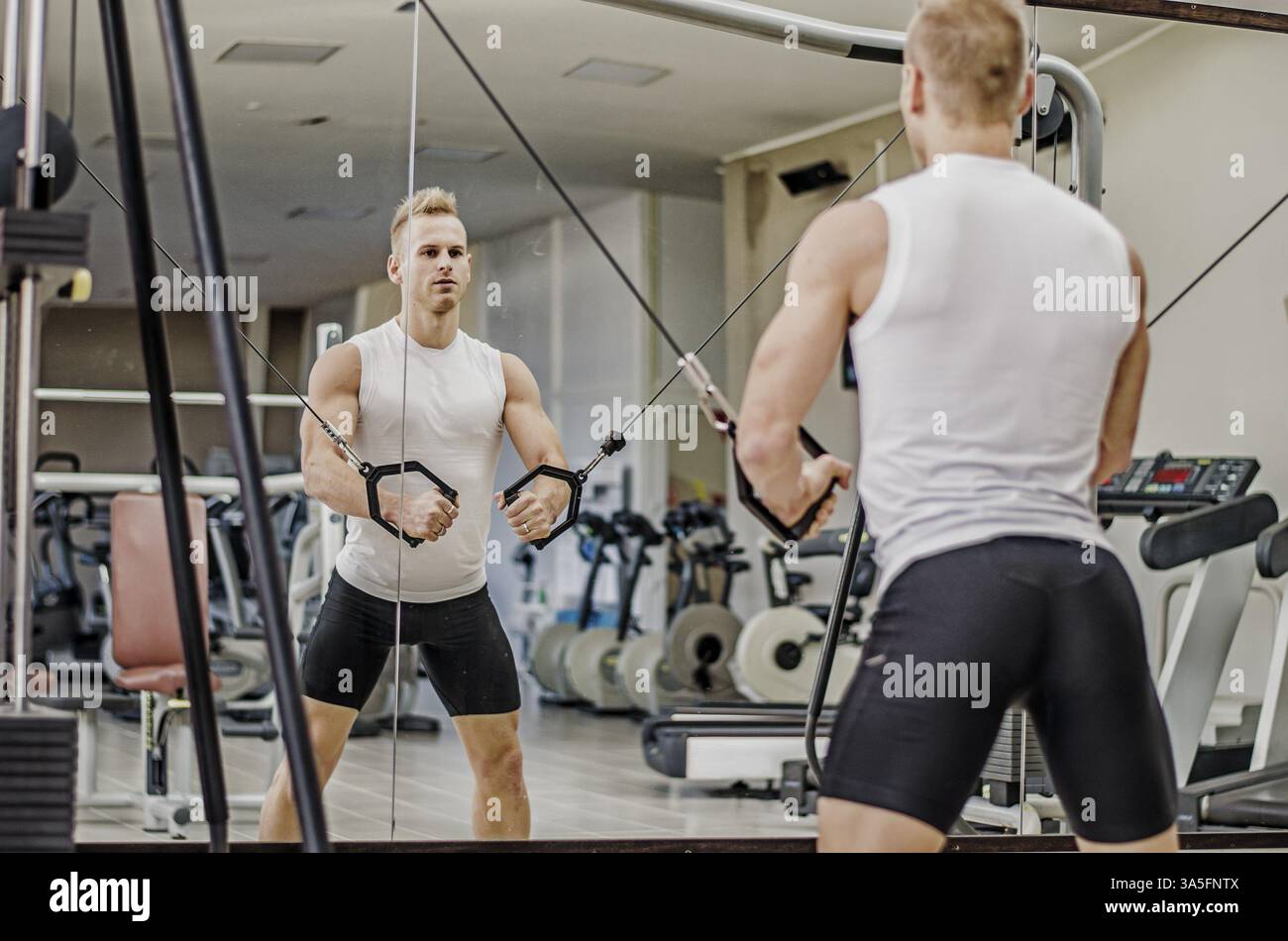 Handsome blond young man exercising pecs on gym equipment, shot from a ...