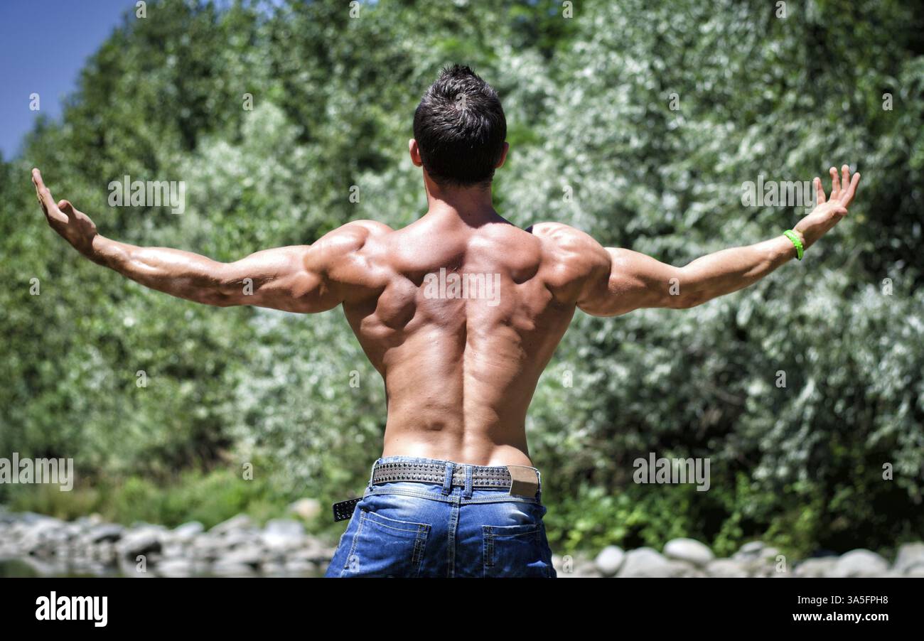 Muscle man in jeans, outdoor with arms spread open, seen from the back ...