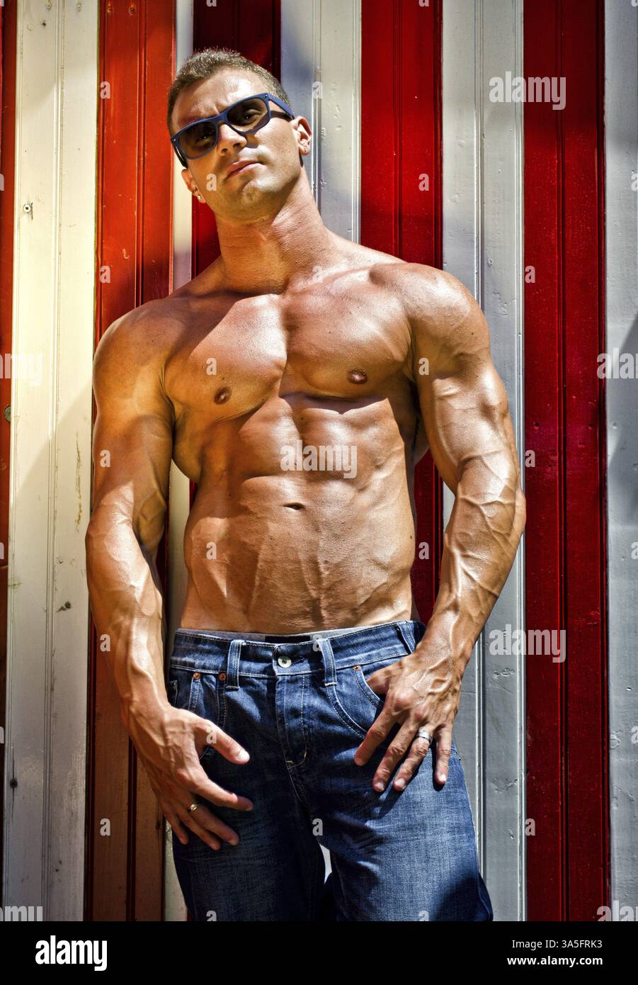 Handsome and muscular male bodybuilder against red and white beach ...