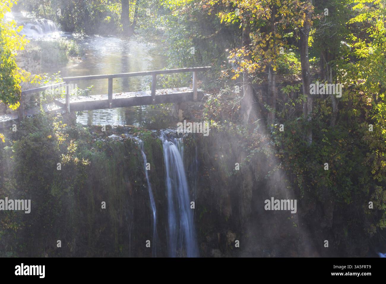 Sun rays over a wooden bridge and a waterfall. The small Croatian town ...