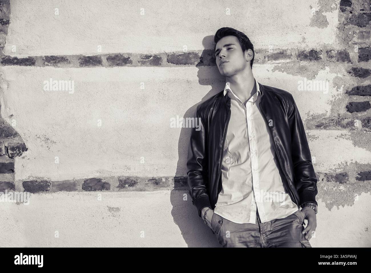 Handsome young man standing in white t-shirt and black leather jacket ...