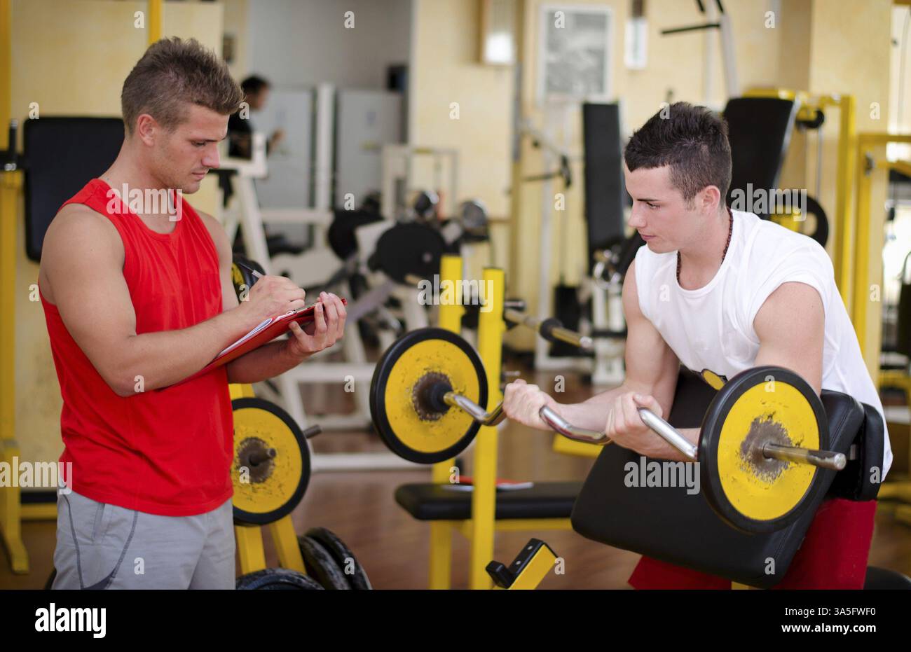 Personal trainer helping young male client in gym during workout on ...