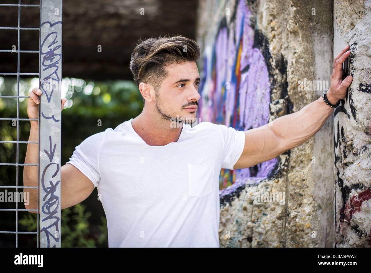 Attractive muscle man leaning on colorful graffiti wall, wearing white ...