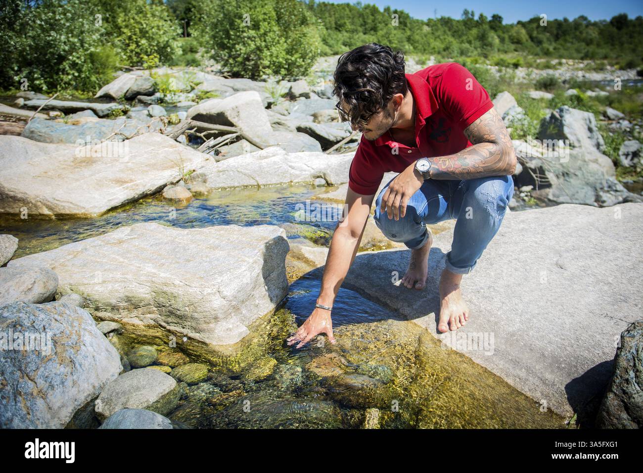 Attractive young man outdoor at river or water stream, sitting on big ...