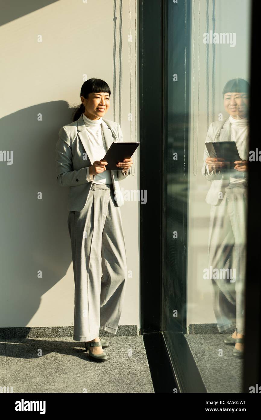 Japanese woman in a tailored gray suit stands by a large window ...